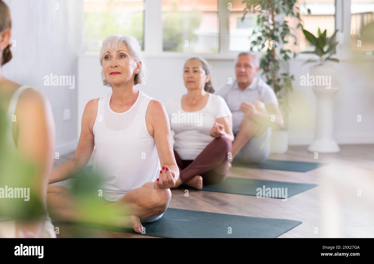 In yoga class senior lady performs lotus pose-Padmasana-Siddhasana with ...
