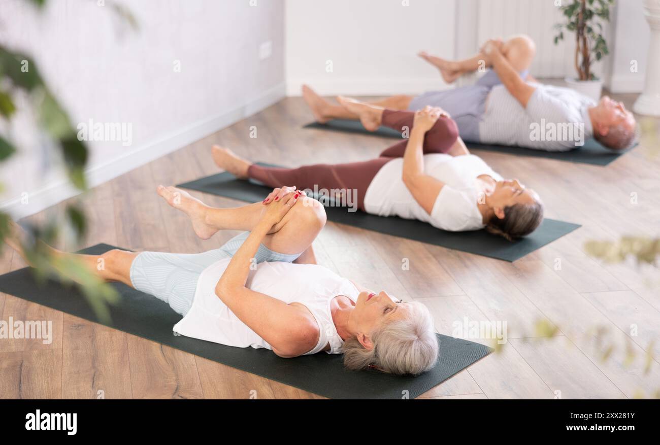 Class of mature women stretching gluteal muscle while lying on back ...