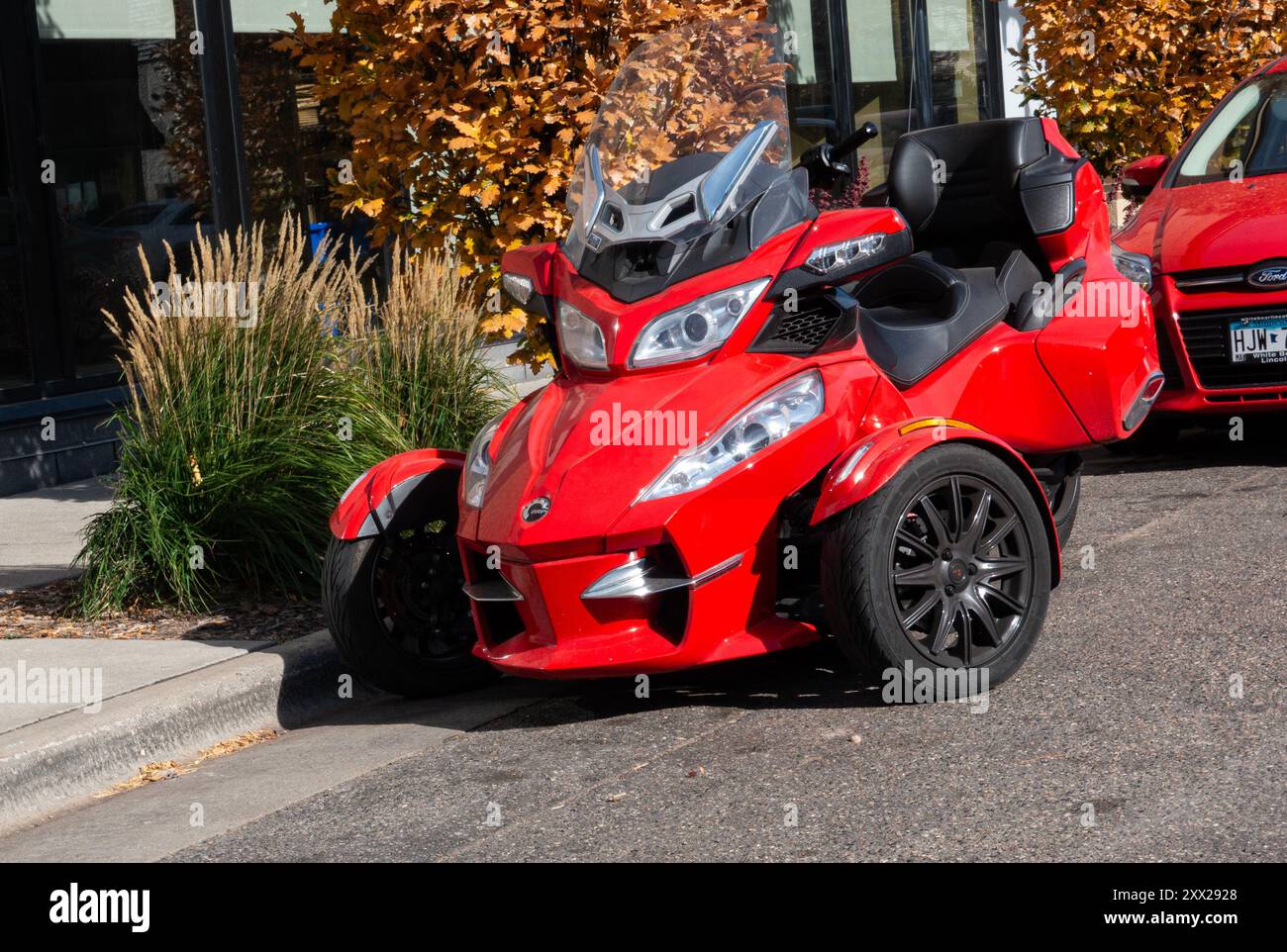 Red BRP three wheel vehicle parked at the curb on a city street. St ...