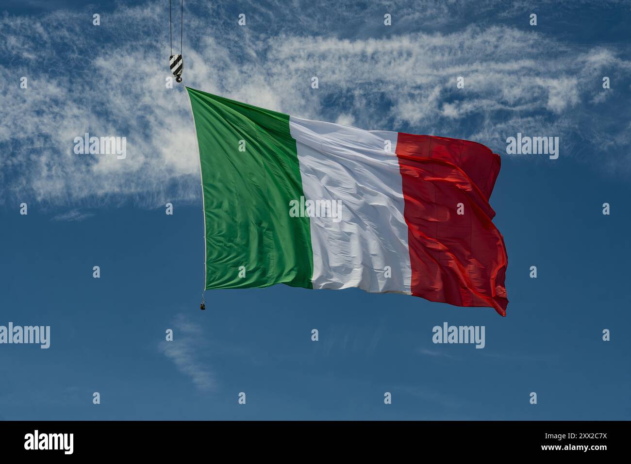 A large Italian flag waving in the sky supported by a crane hook ...