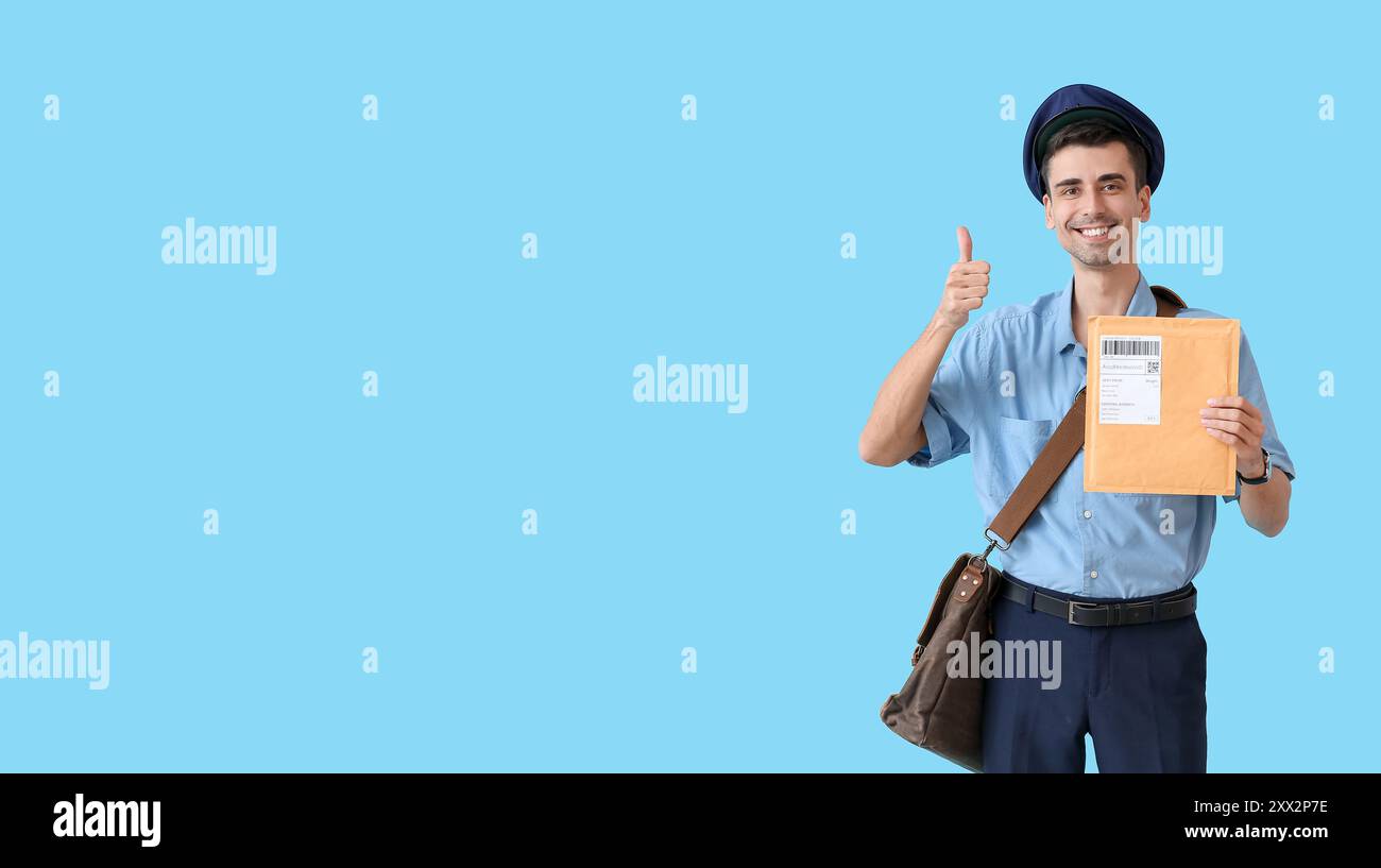 Handsome young postman with letter showing thumb-up on light blue ...