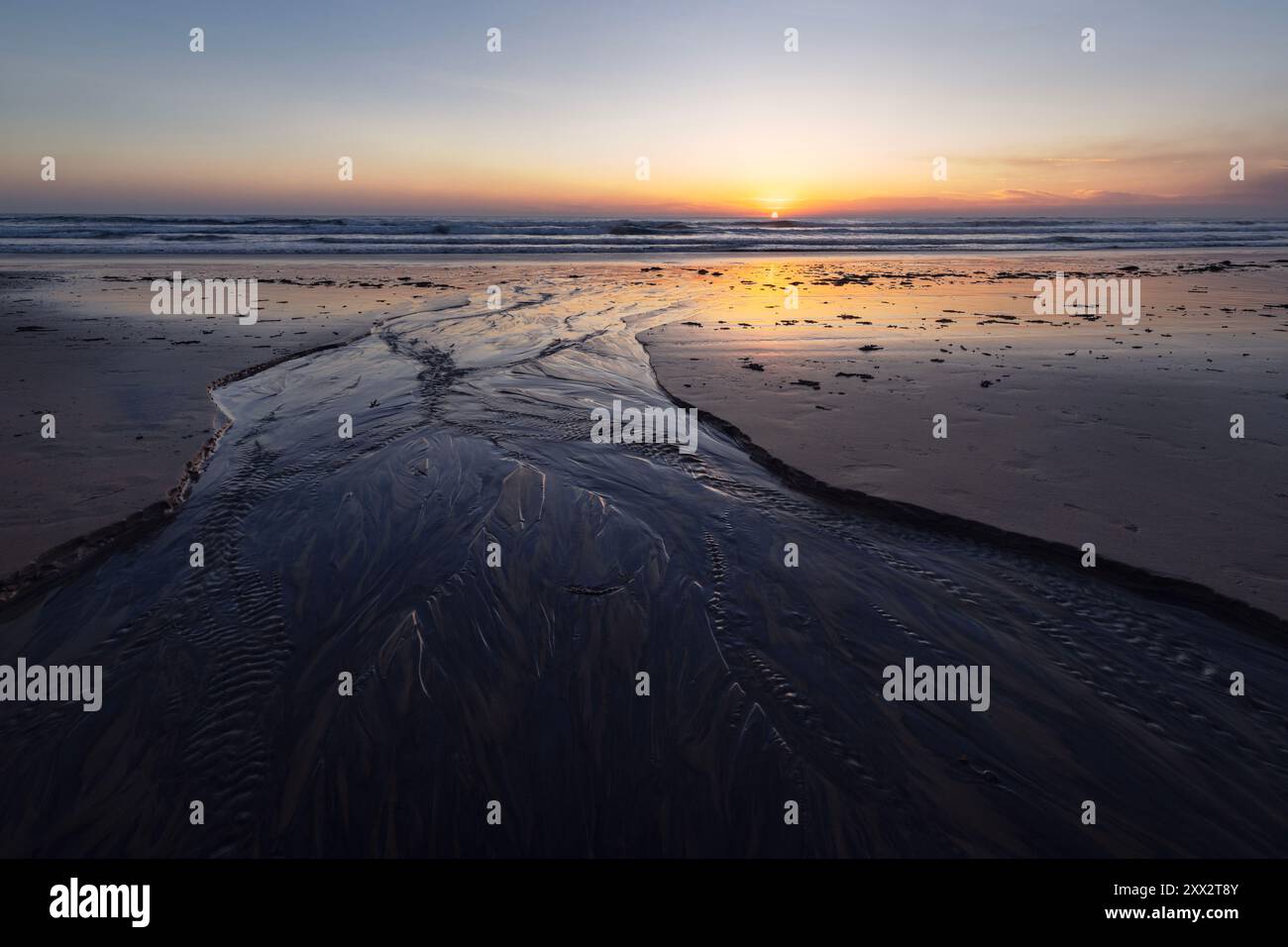 creek flowing through sand out to ocean during a sunset over a beach at ...