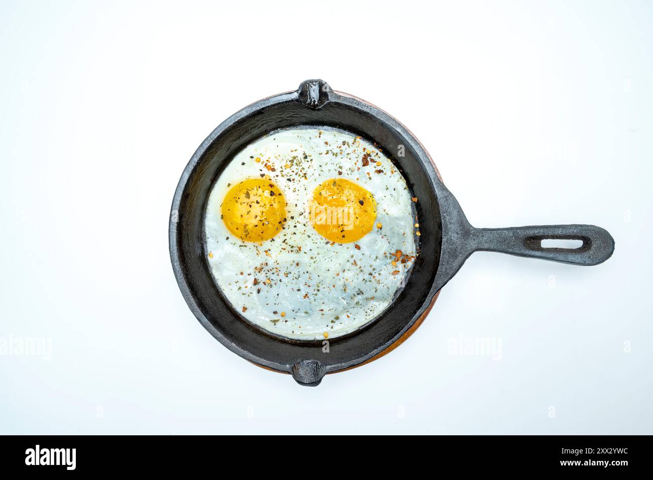A pan with sunny side up eggs and some pepper on top. The eggs are ...