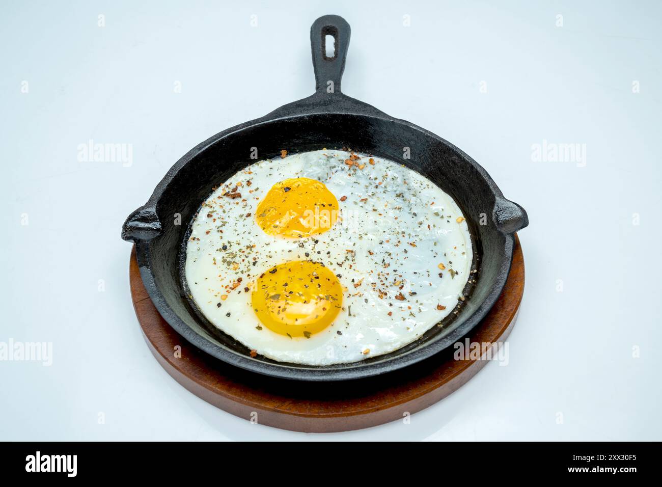 A pan with sunny side up eggs and some pepper on top. The eggs are ...