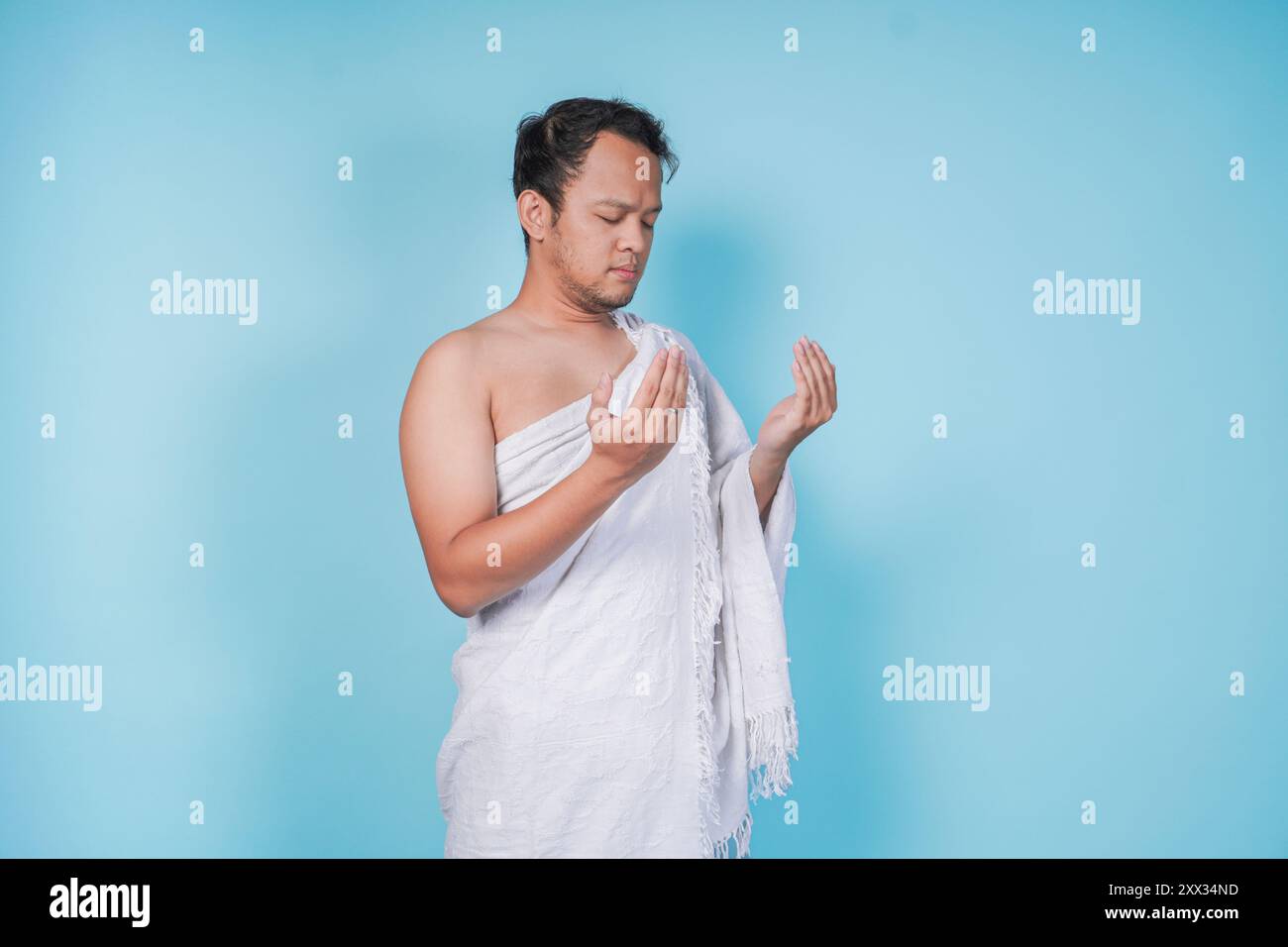 Portrait of young Asian Muslim man wearing ihram praying with eyes ...