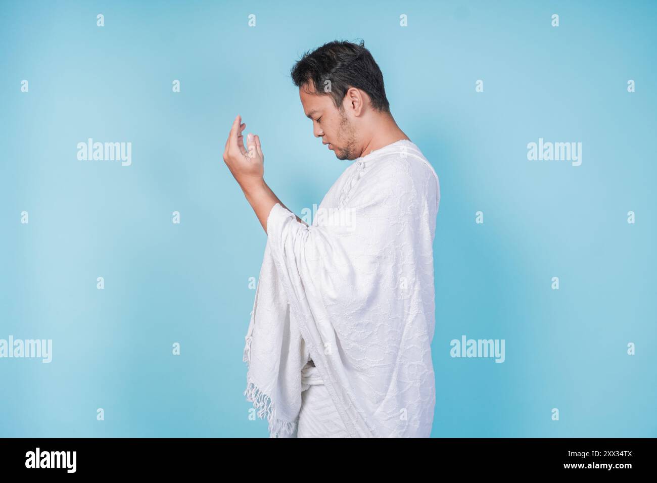 Side portrait of young Asian Muslim man wearing ihram praying with hand ...