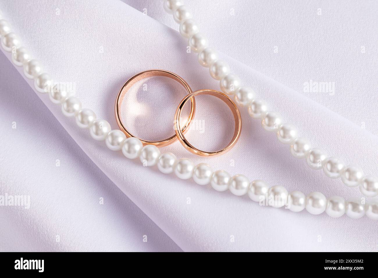 Two elegant gold wedding rings lie on a large fold of white satin among ...