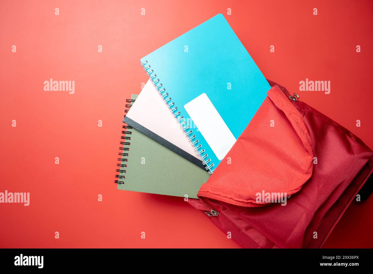 A red backpack with three spiral notebooks inside. The notebooks are ...