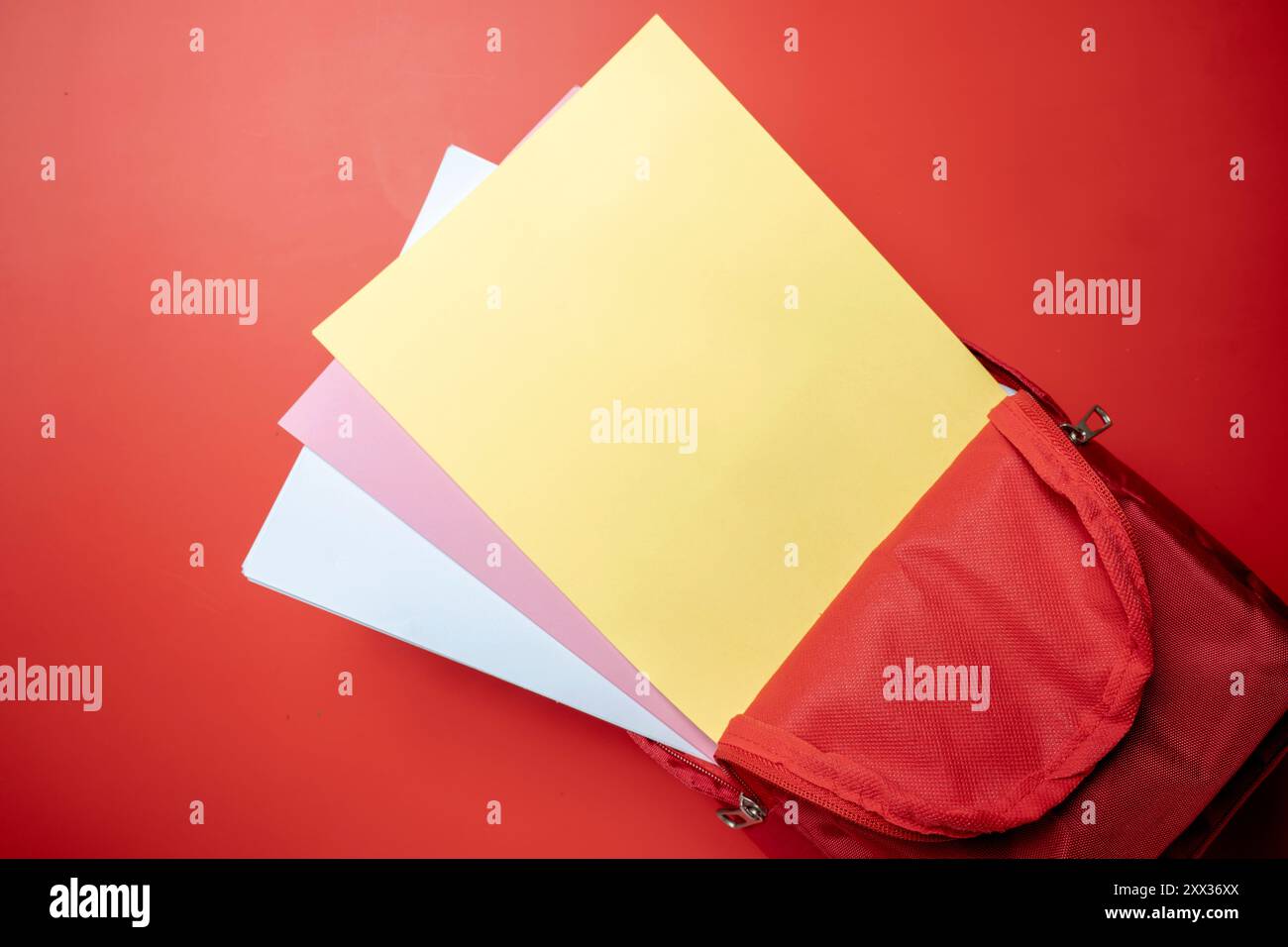 A red backpack with three sheets of paper inside. The backpack is open ...