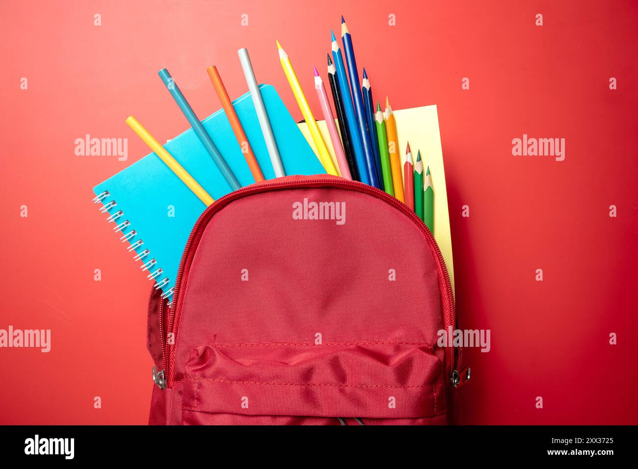 A red backpack with a bunch of pencils and notebooks inside. The ...