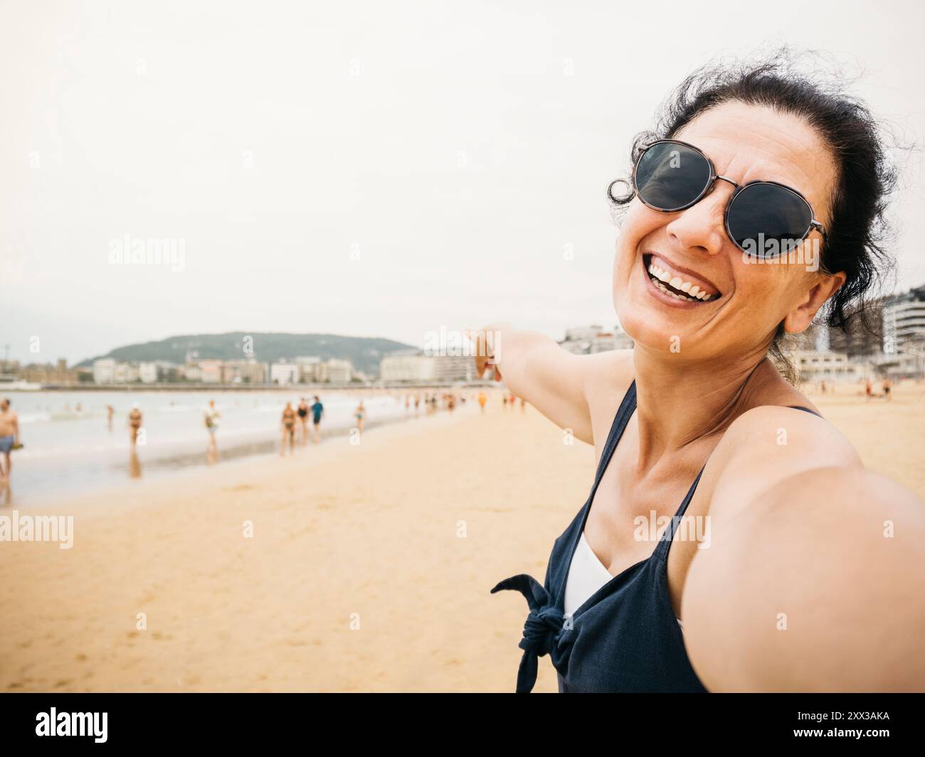 Joyful woman taking a selfie on the beach, pointing at the view behind ...