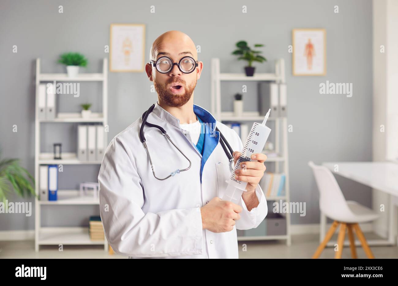 Funny young man doctor holding big syringe standing in medical clinic ...