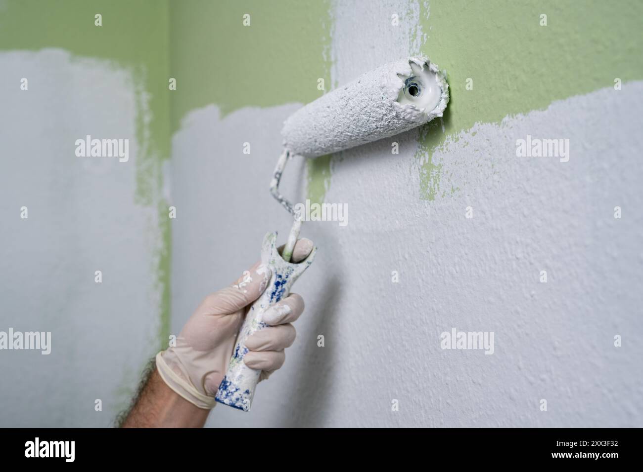 A man's hand paints a green wall in room with a roller in white paint ...
