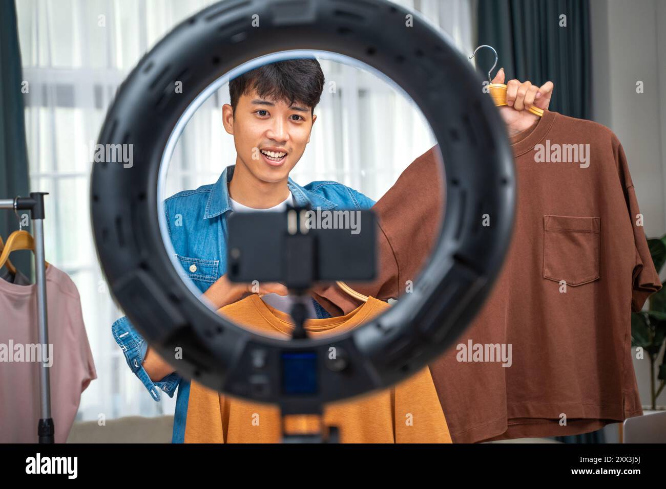 Young online seller man showing his shirt product during online live streaming from his home ...