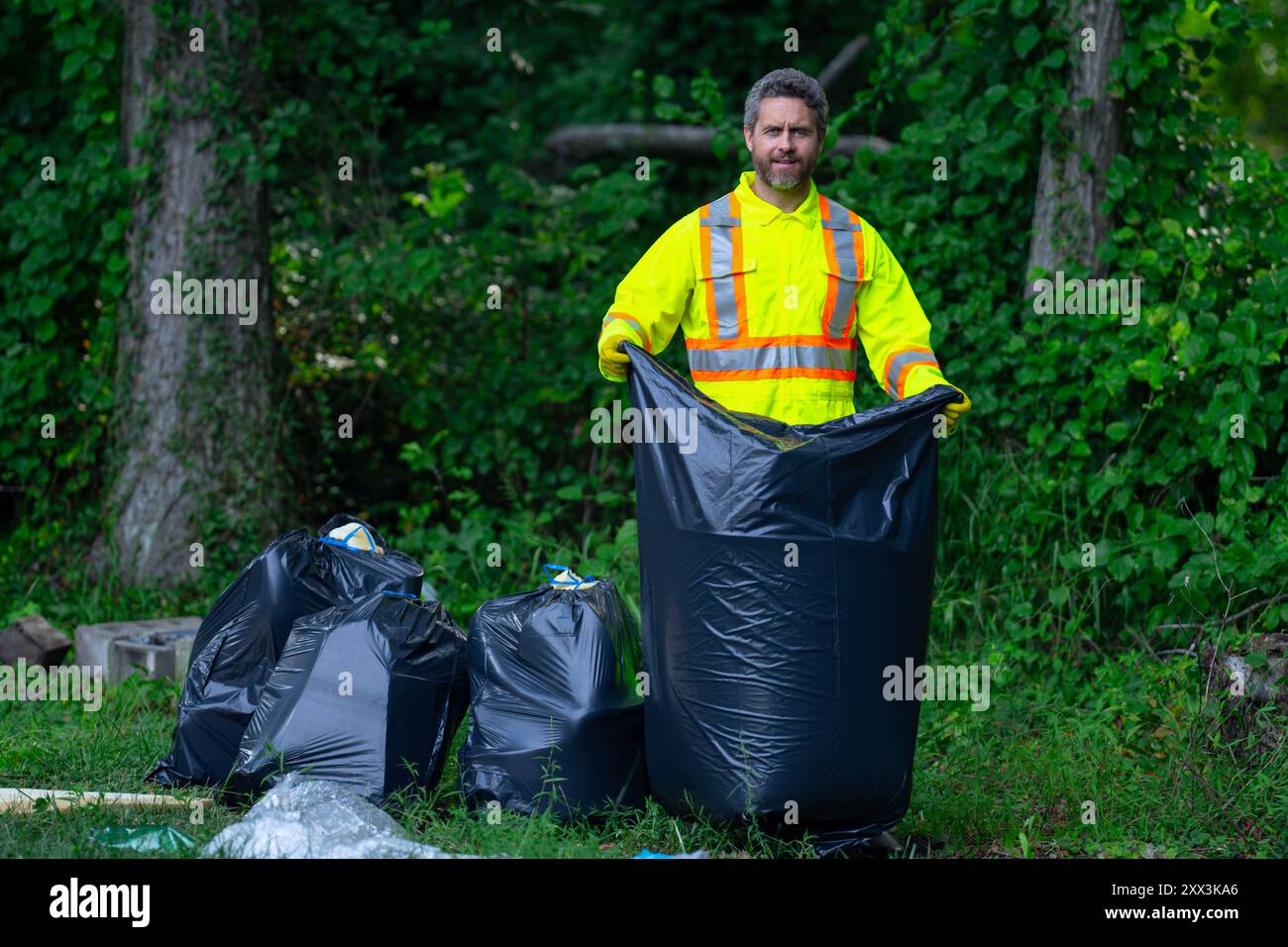 Volunteer man collecting garbage, picking up waste at nature. Land pollution, environmental ...