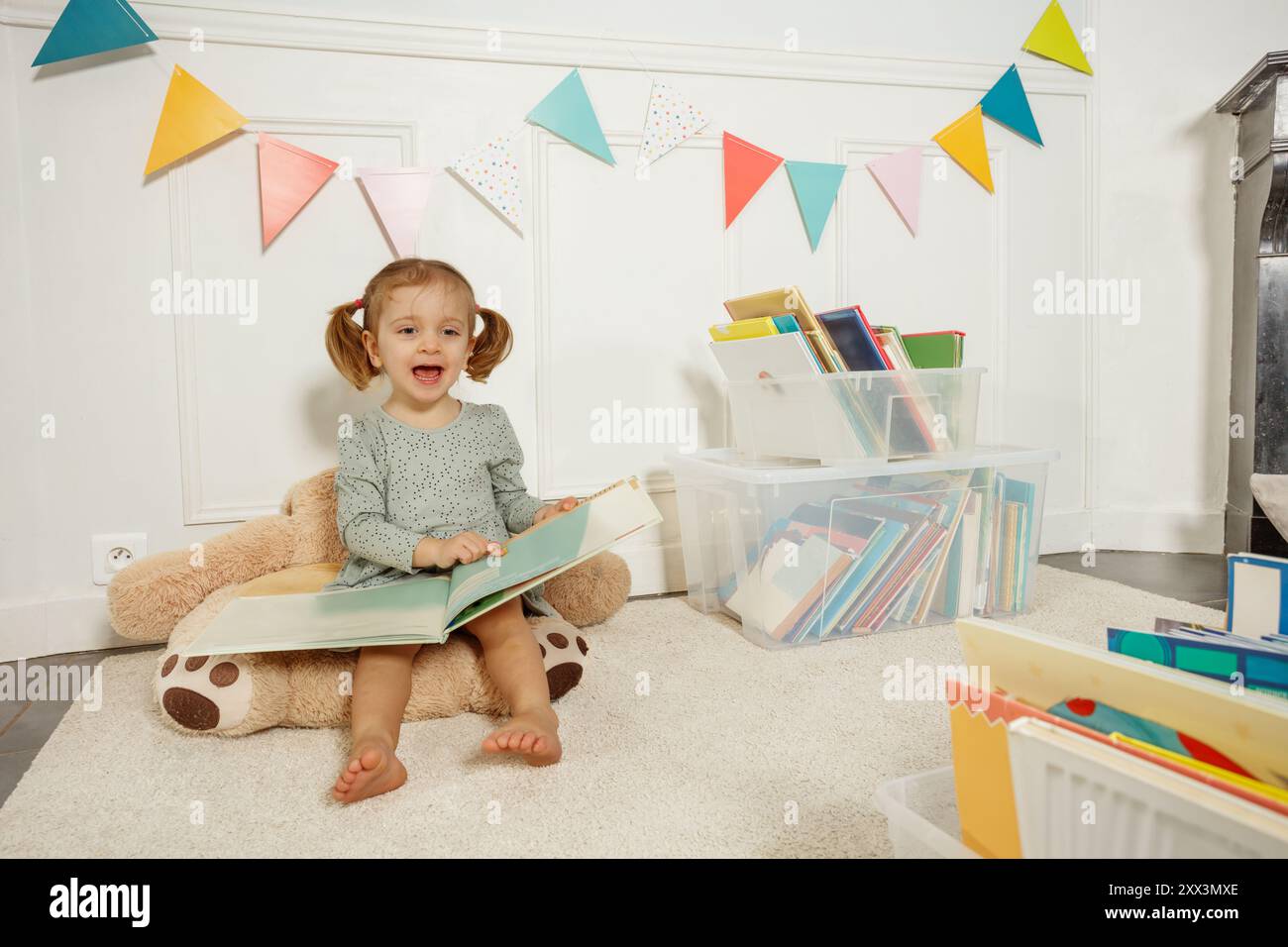 Little girl enjoys reading while resting on her large teddy bea Stock ...