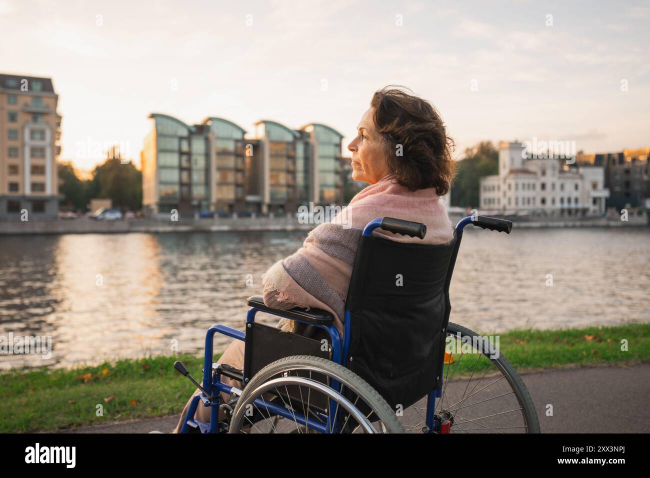 Sad senior woman sitting in wheelchair walking on road in city outdoor ...