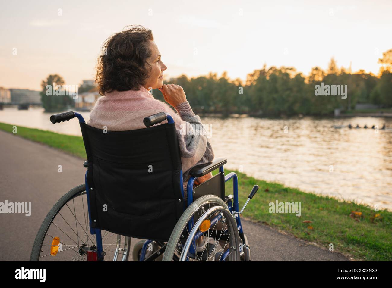 Sad senior woman sitting in wheelchair walking on road in city outdoor ...
