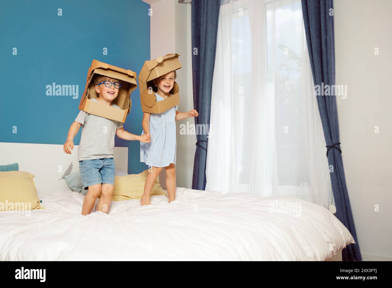 Two children with box helmets hop joyfully on a cozy white bed Stock ...