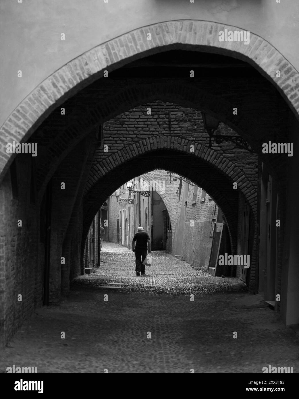 A man with a shopping bag walks alone under an archway in an old town ...