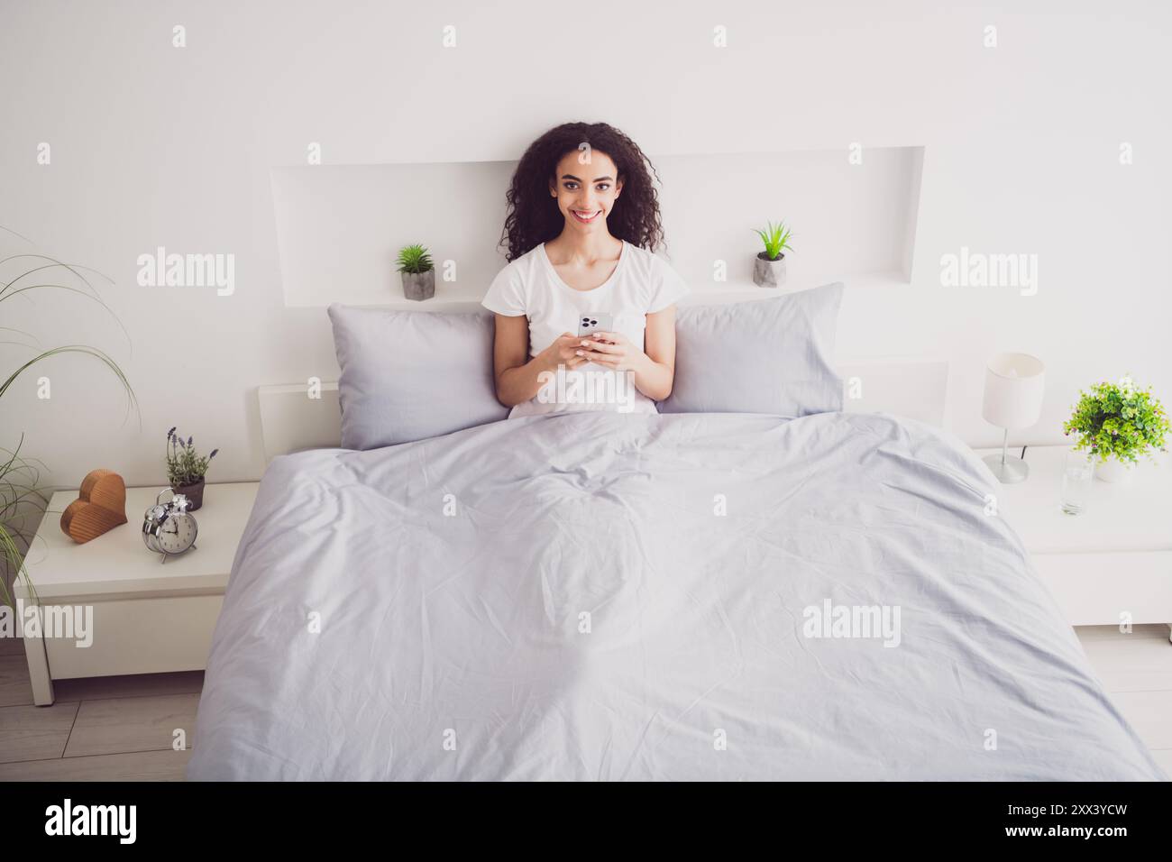 Photo of charming young woman lying bed hold device good morning vibes awake home bedroom light ...