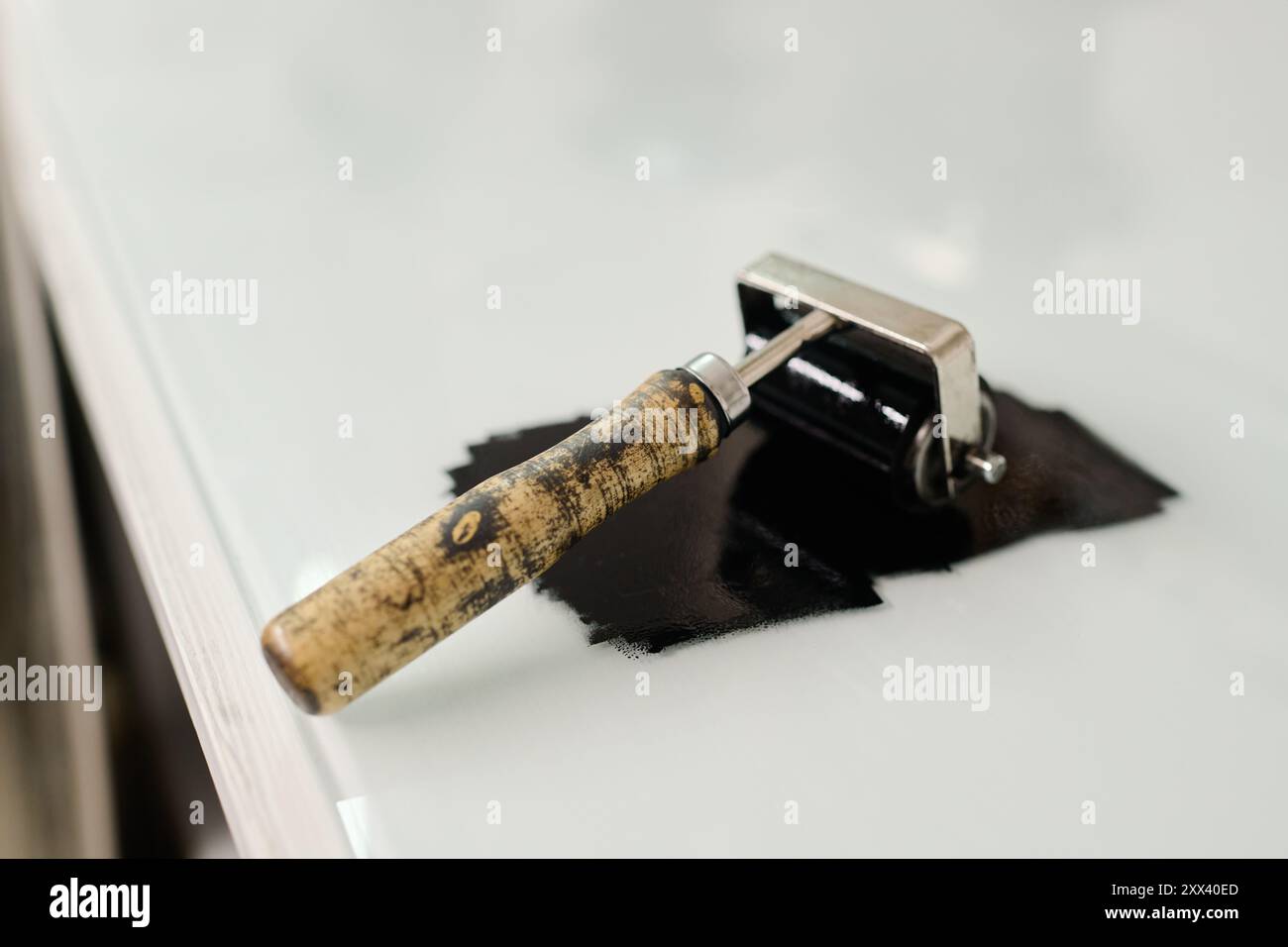 Handtool with wooden handle and narrow roller lying on black ink ...