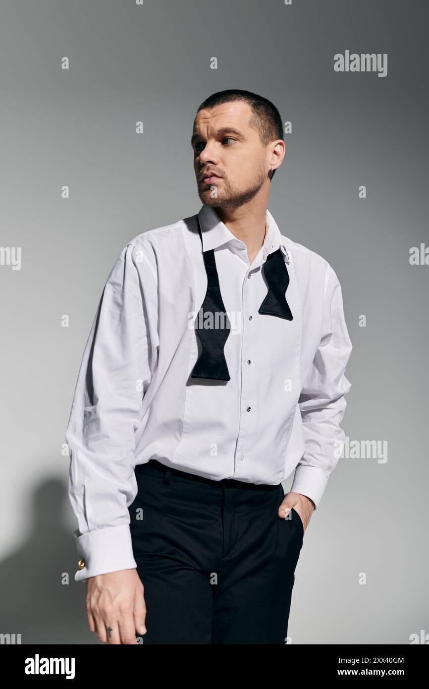 A stylish man in a white shirt and black bow tie poses against a grey ...