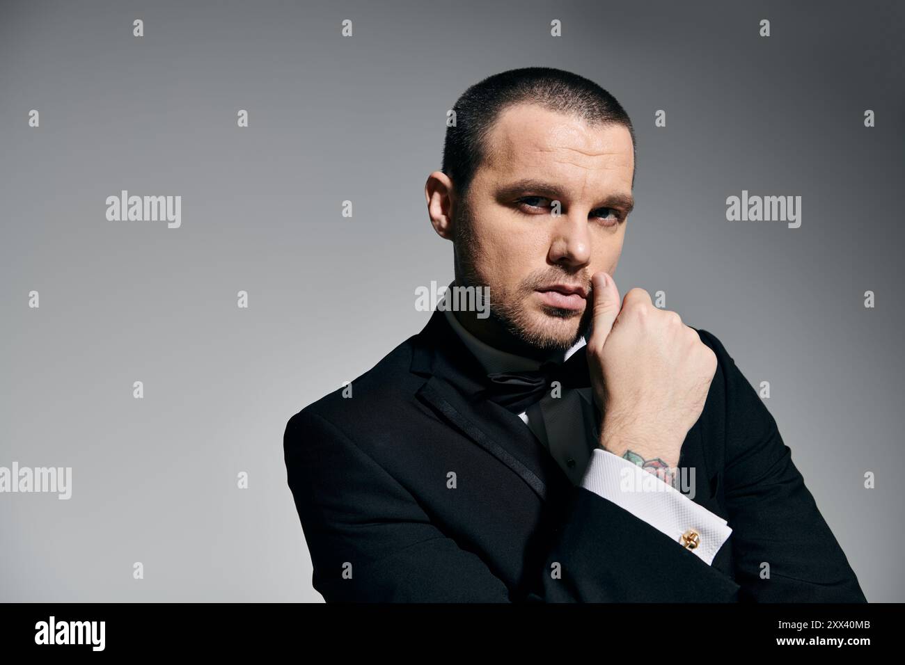 A man in a tuxedo, with a sharp haircut and thoughtful gaze, poses ...