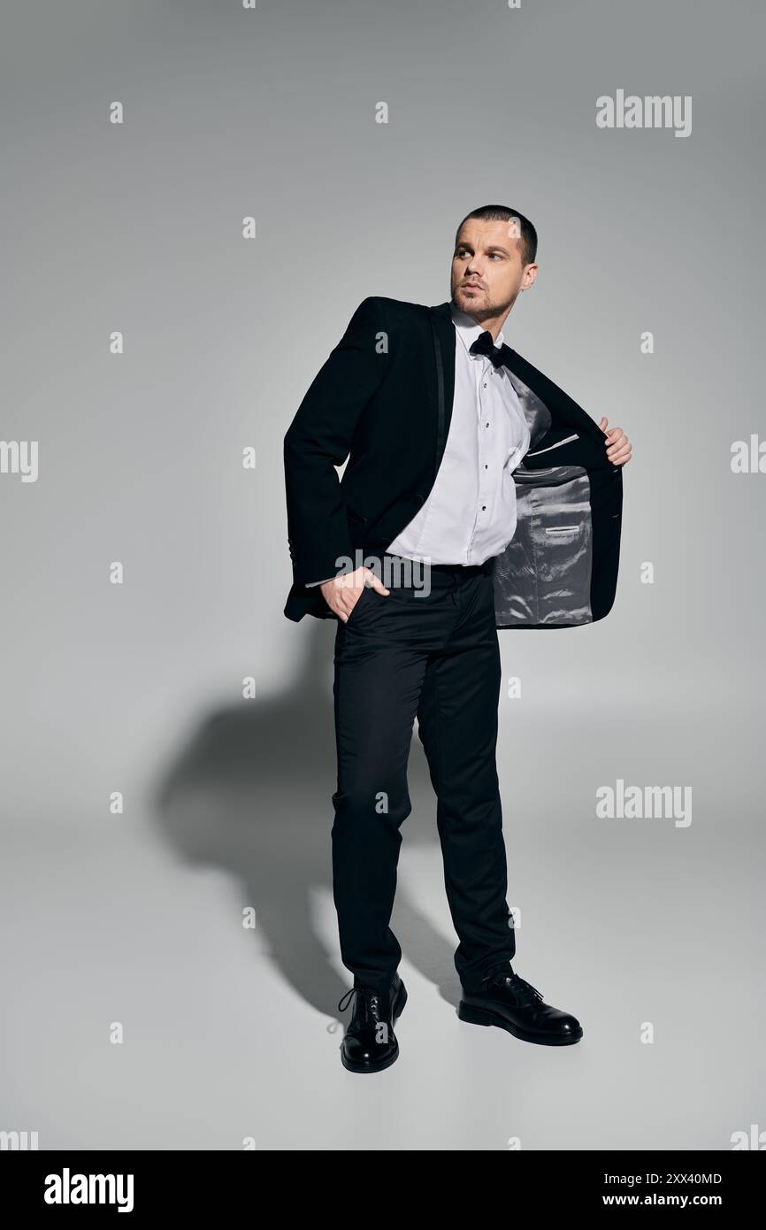 A man in a black tuxedo with a bow tie stands confidently, holding his ...