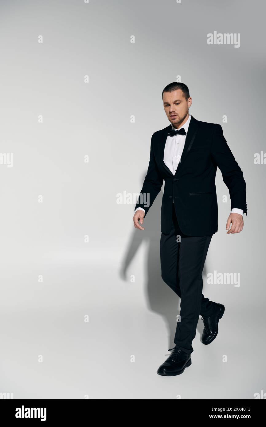 A dapper man in a black tuxedo walks confidently across a white studio ...