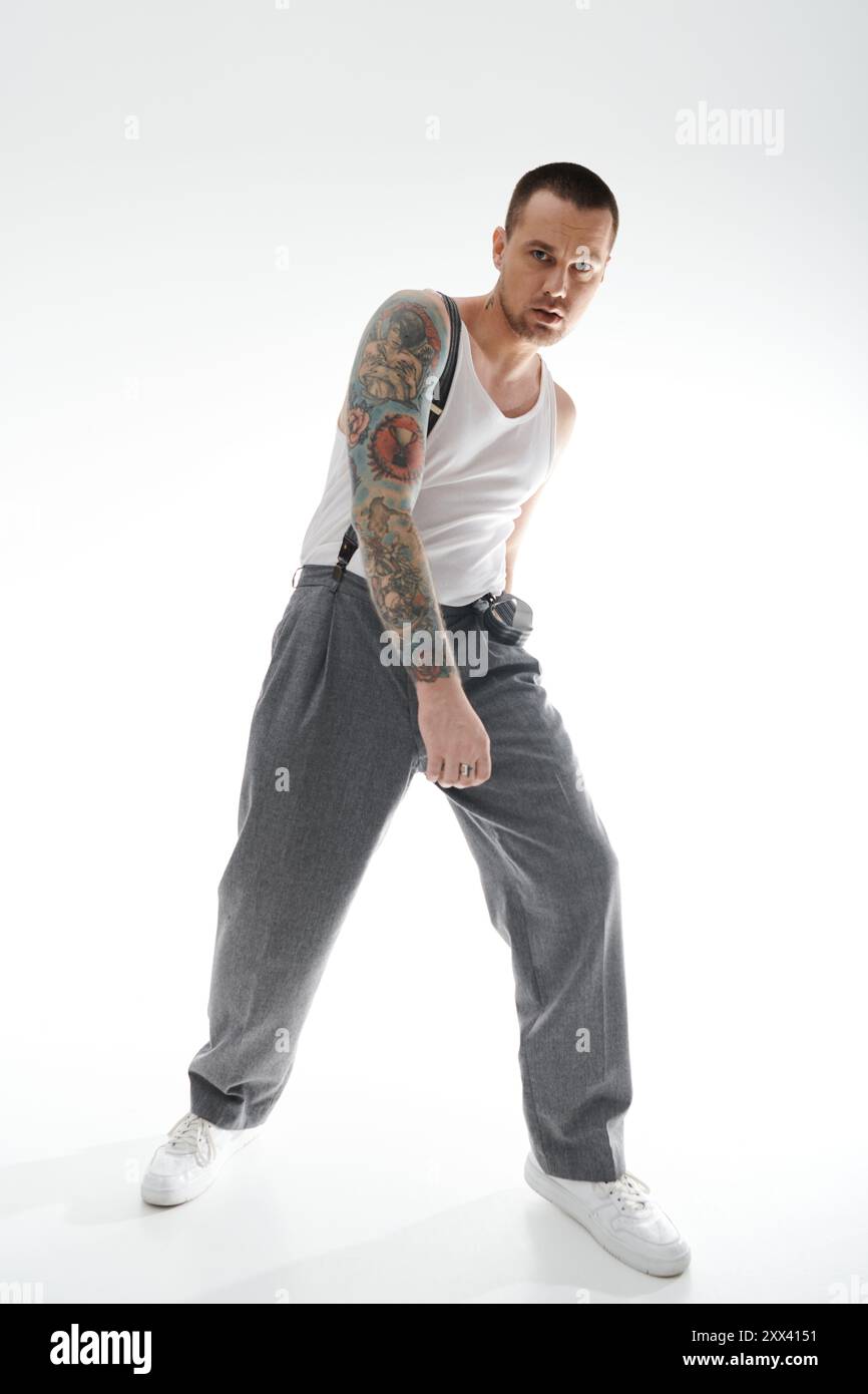 A man in suspenders and a white tank top poses against a white ...