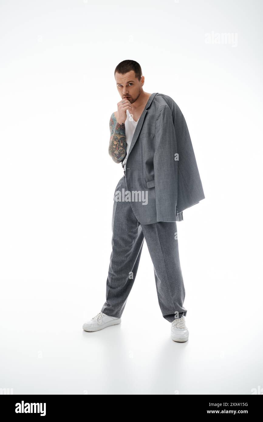 A stylish man in a grey suit with his jacket slung over his shoulder ...