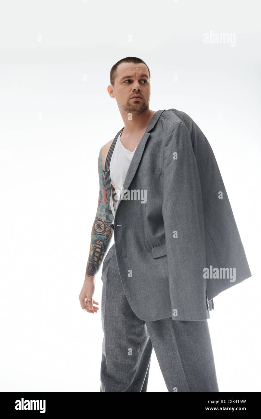Stylish man in grey suit confidently poses with jacket over shoulder ...