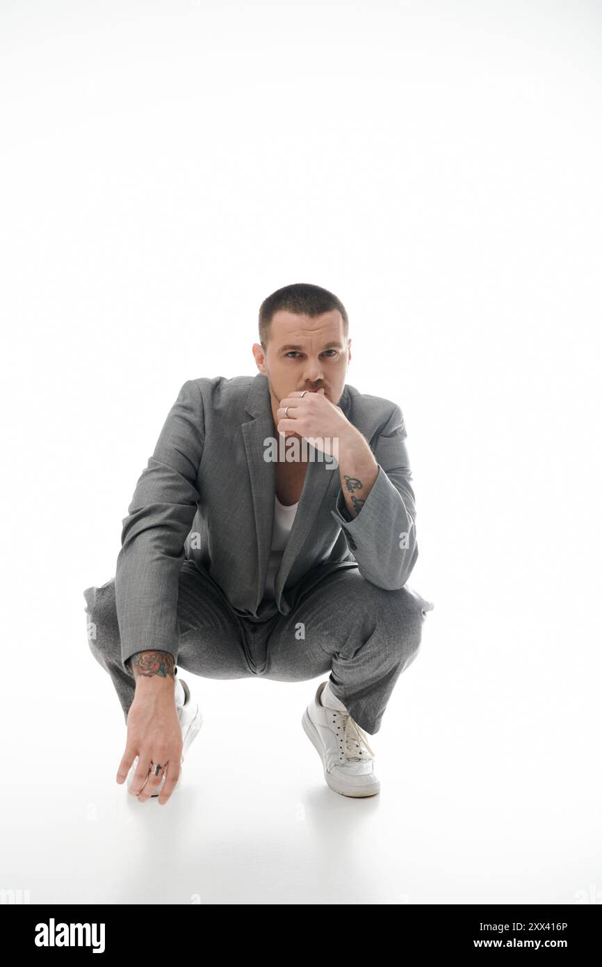 A man in a gray suit and white sneakers sits in a squat position Stock ...