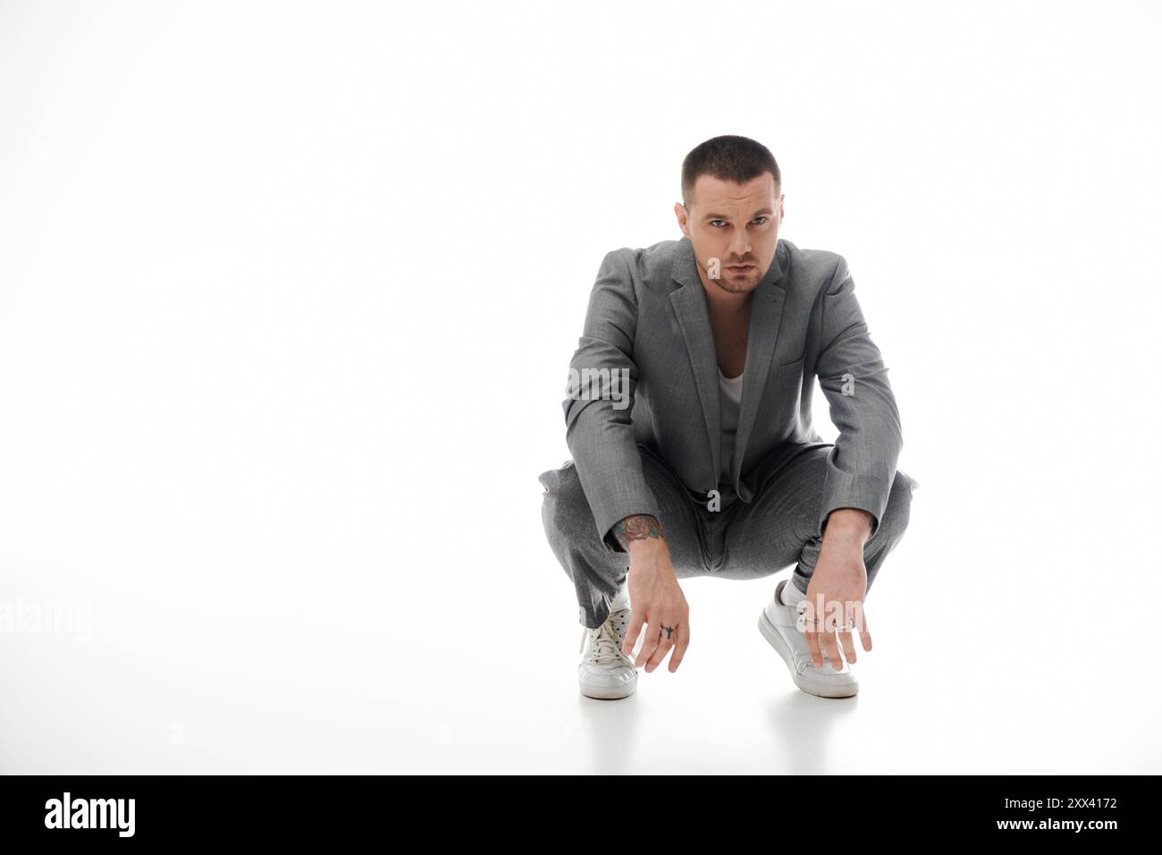 Stylish man in grey suit, squatting, hands on knees, looking at camera ...