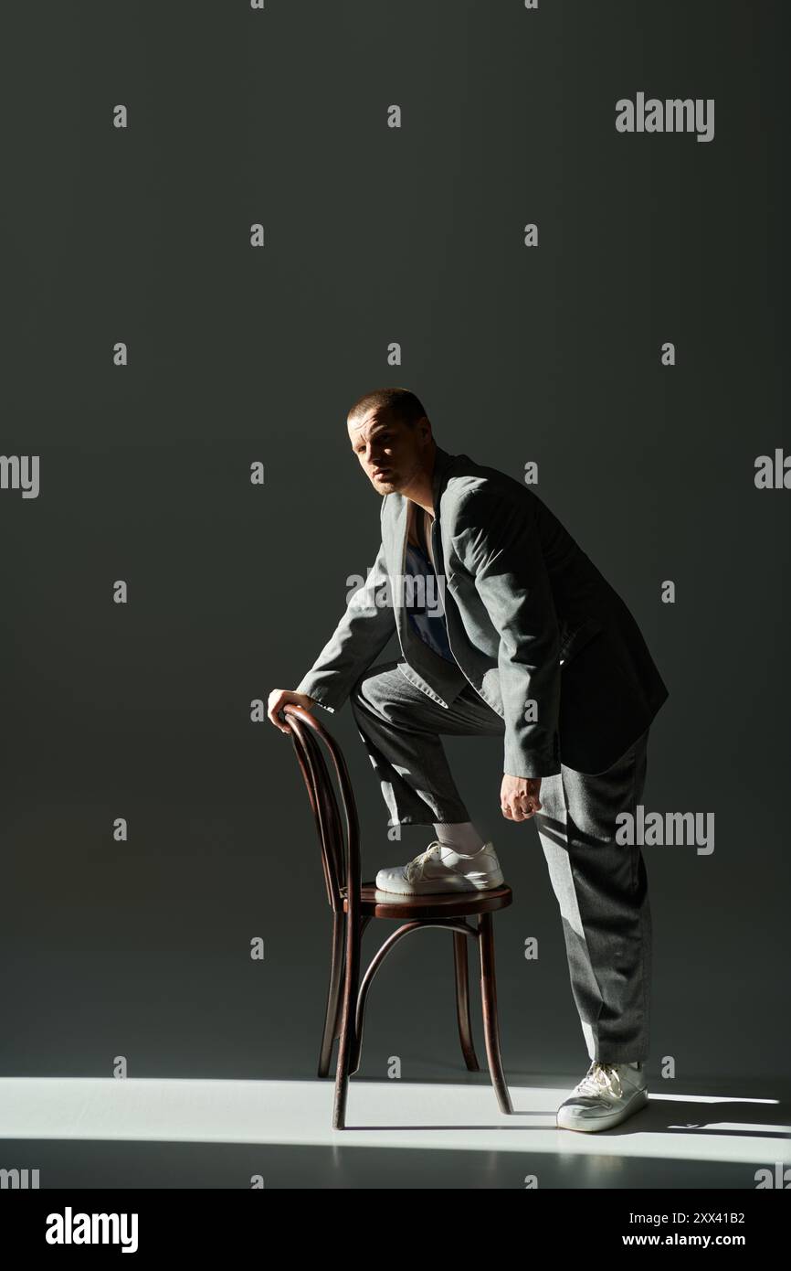 A man in a grey suit leans on a chair in a studio setting Stock Photo ...