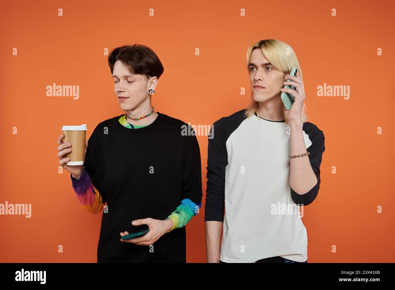 Two young queer friends pose in vibrant attire against an orange ...