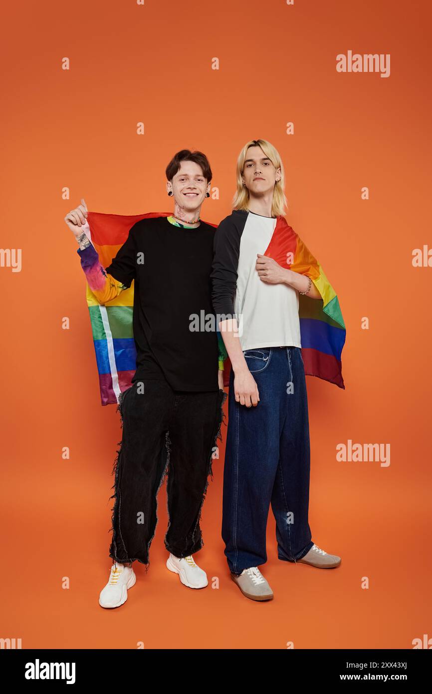Two young queer friends stand together, smiling and holding a rainbow ...