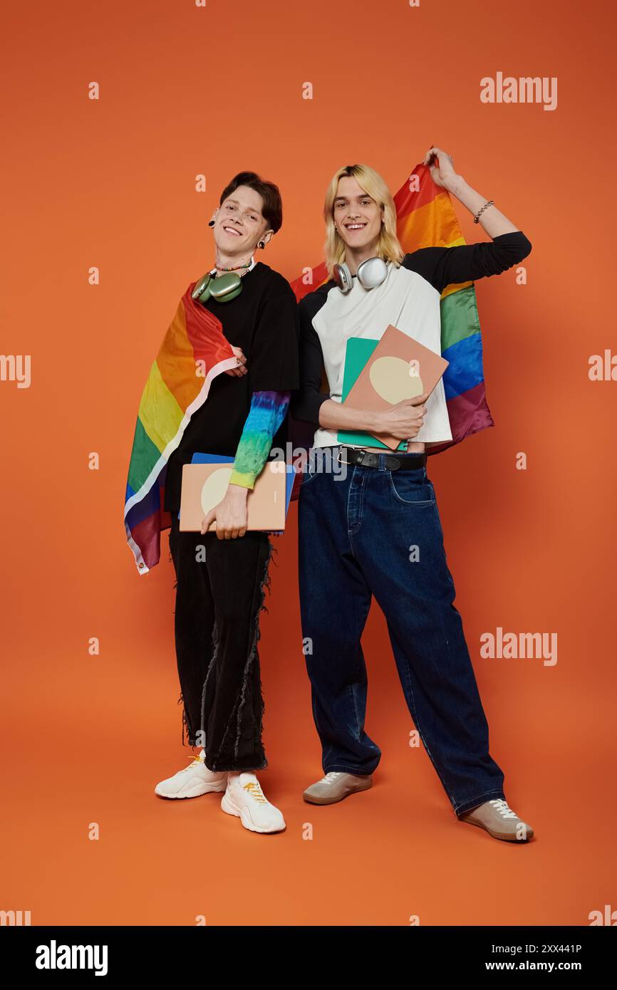 Two young queer friends stand proudly with rainbow flags draped around ...