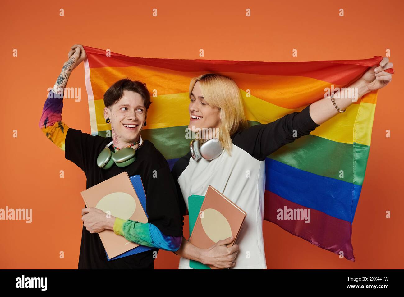 Two young friends hold a pride flag and pose with notebooks in front of ...