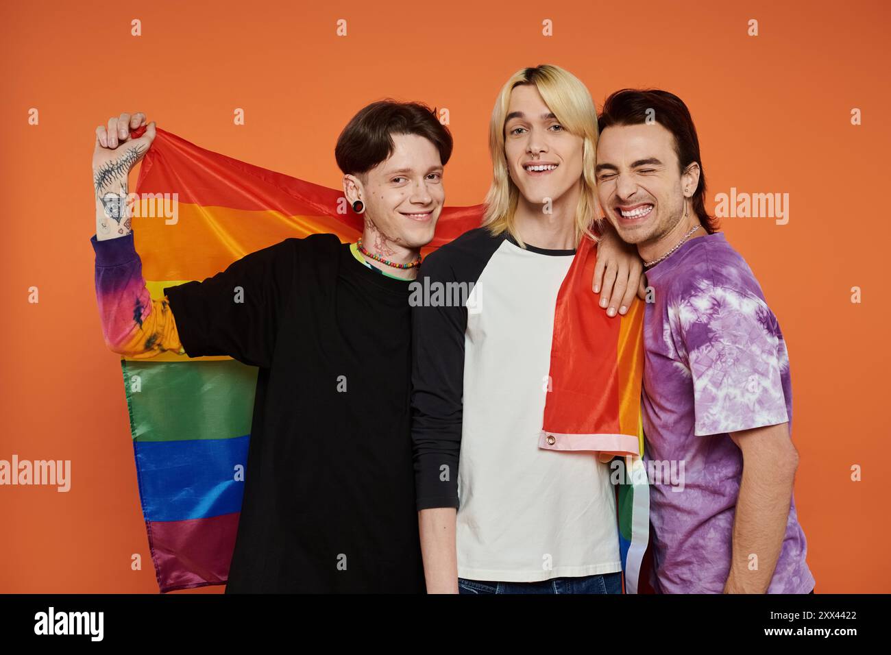 Three young friends stand together, smiling and holding a rainbow pride ...