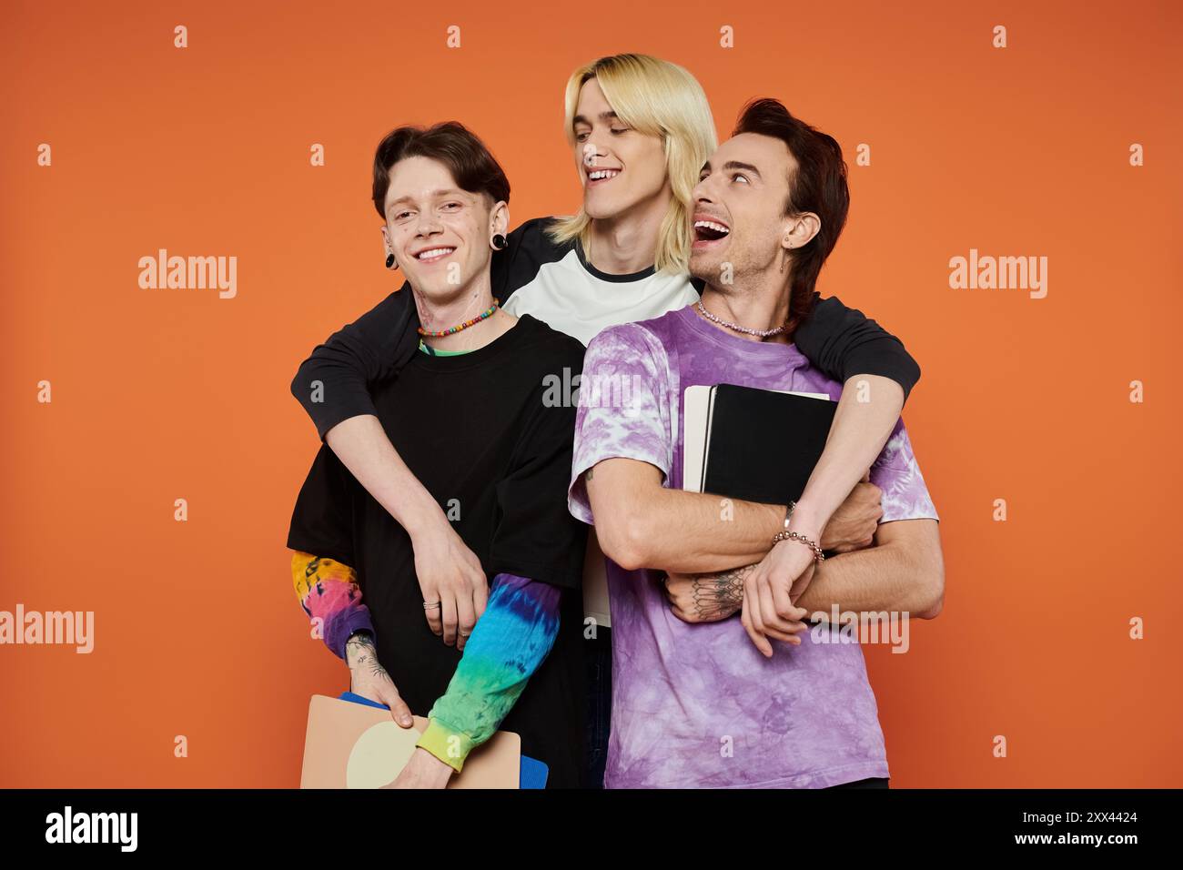 Three young queer friends pose together, smiling and laughing, in front ...