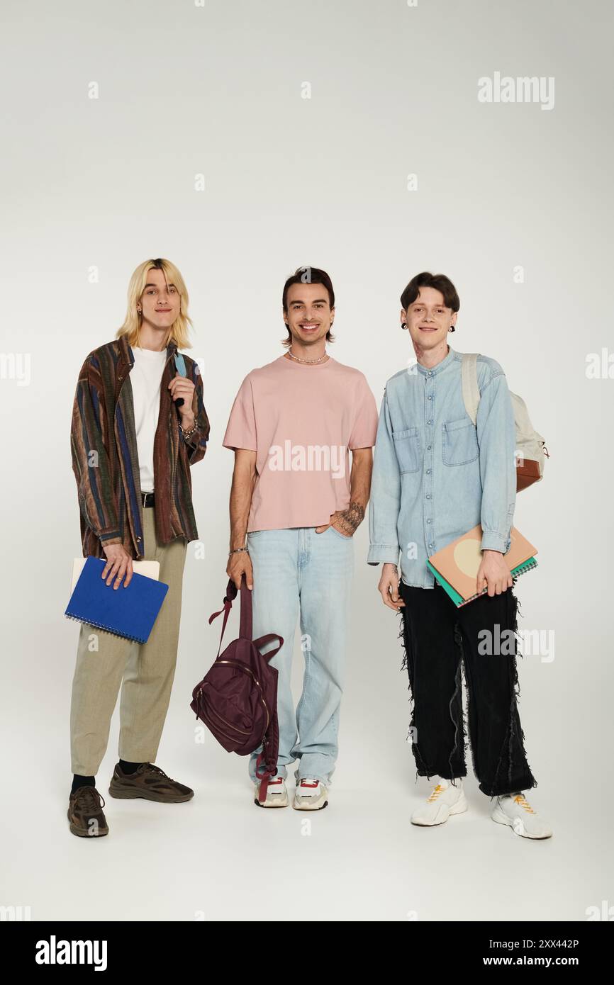 Three young people, dressed casually, stand together in front of a grey ...