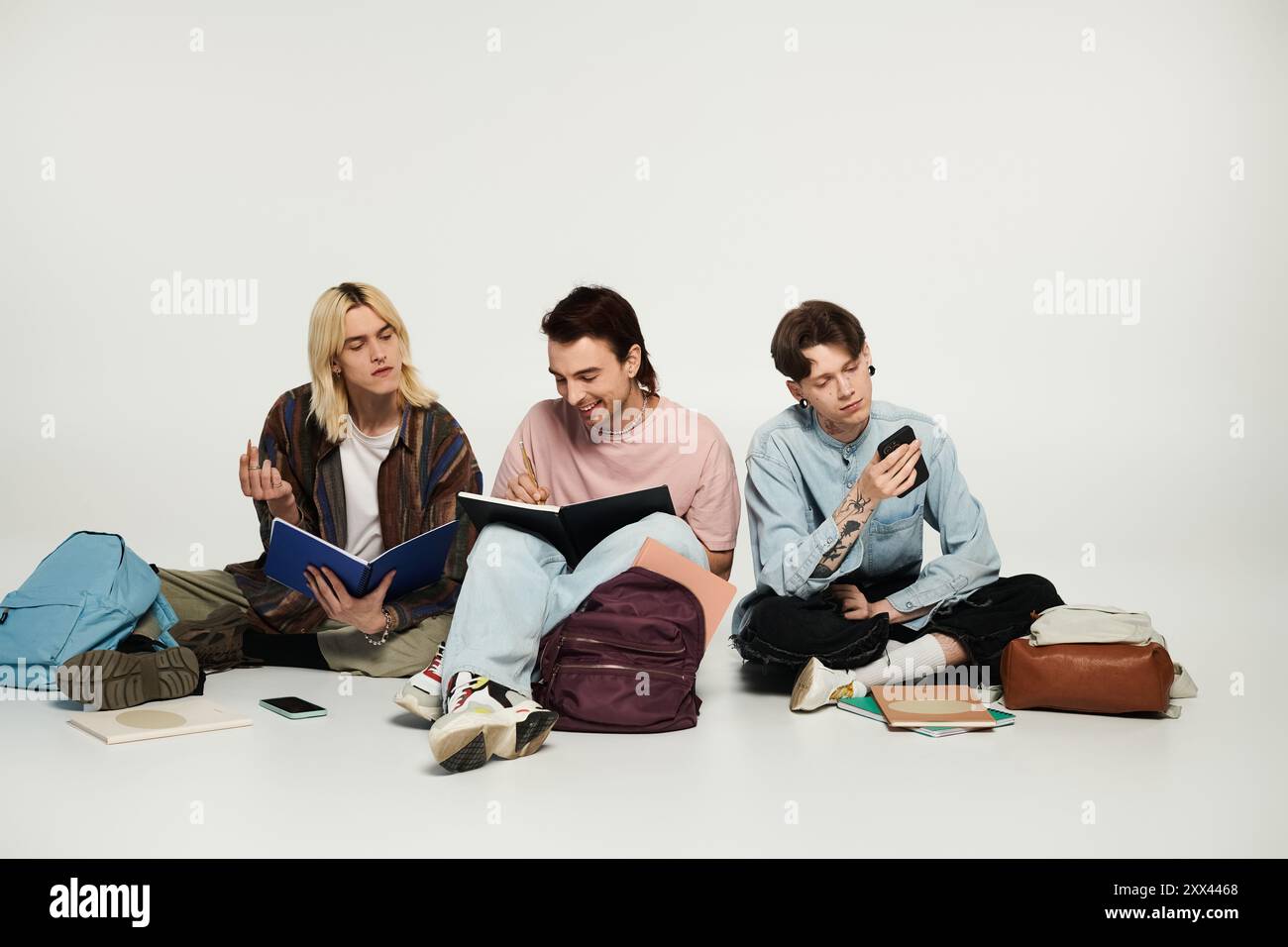 Three young queer students sit on a grey background, studying and ...