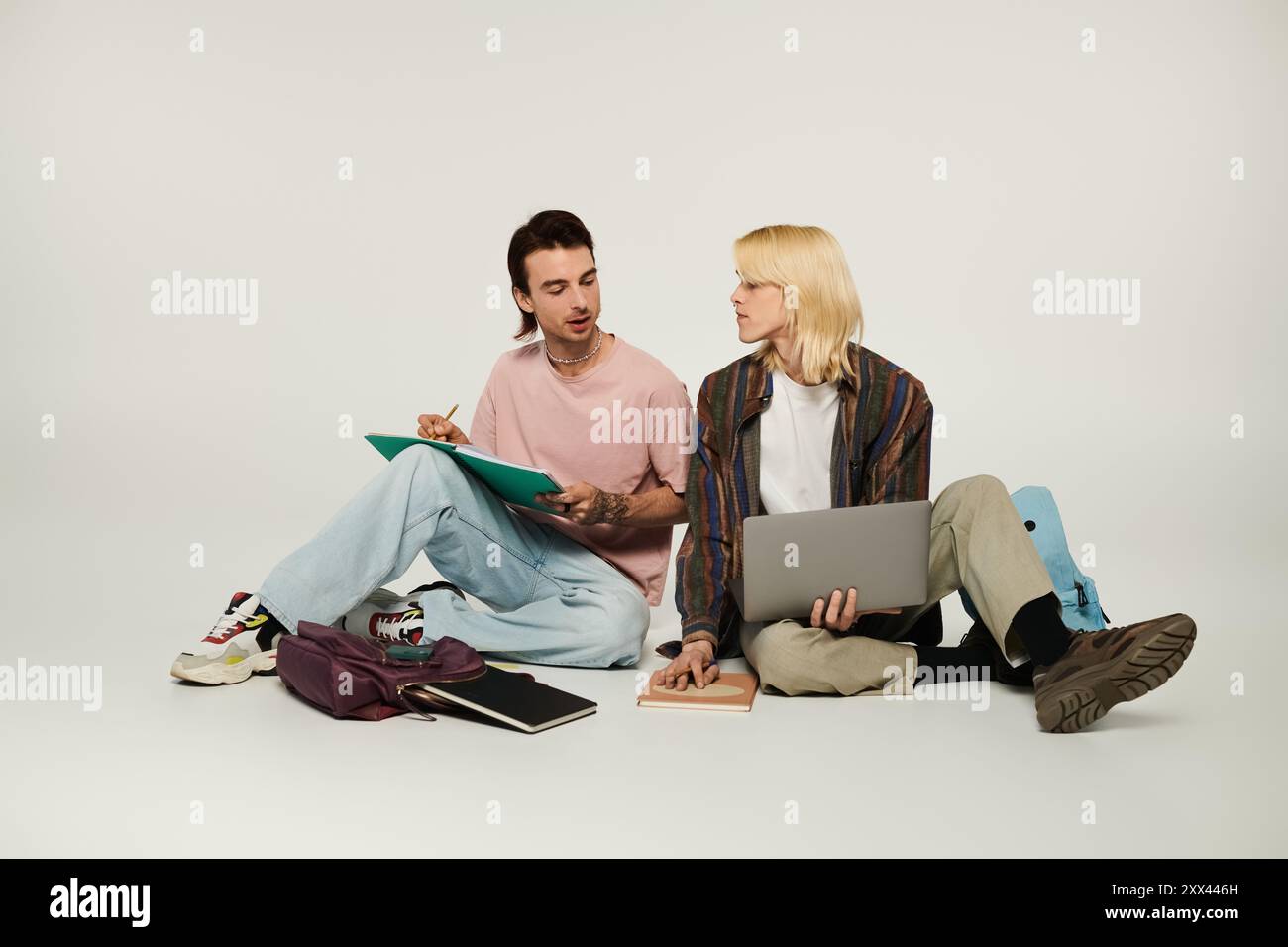 Two young queer students are sitting on the floor, studying together ...