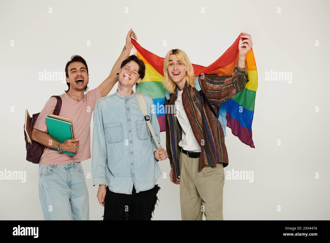 Three young students stand together, holding a rainbow flag, expressing ...