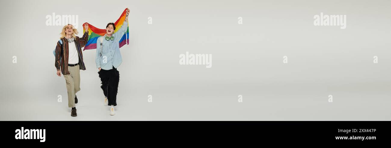 Two young students holding a rainbow pride flag and walking towards the ...