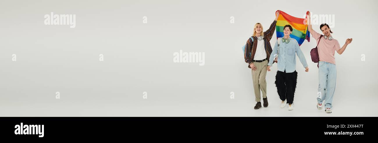 Three young students pose with a rainbow pride flag on a white ...