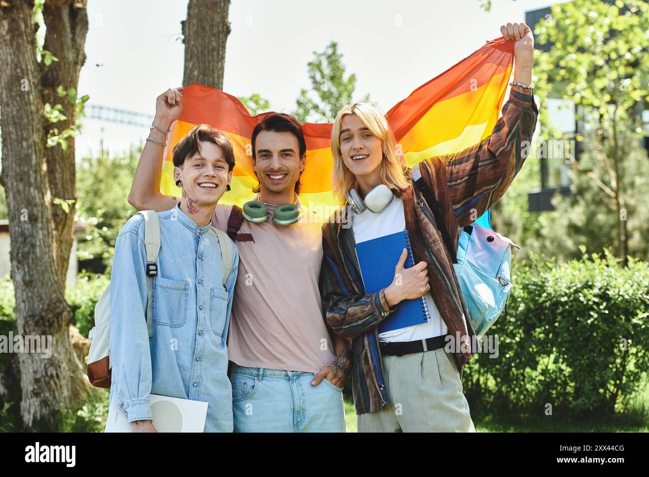 Three young queer friends smile and hold a pride flag in an outdoor ...