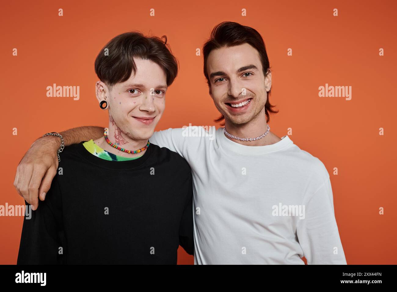 Two young queer friends pose together in vibrant attire against a bold ...